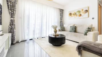 Uma sala de estar moderna com um sofá, uma mesa de centro redonda preta e uma janela grande com cortinas leves.
