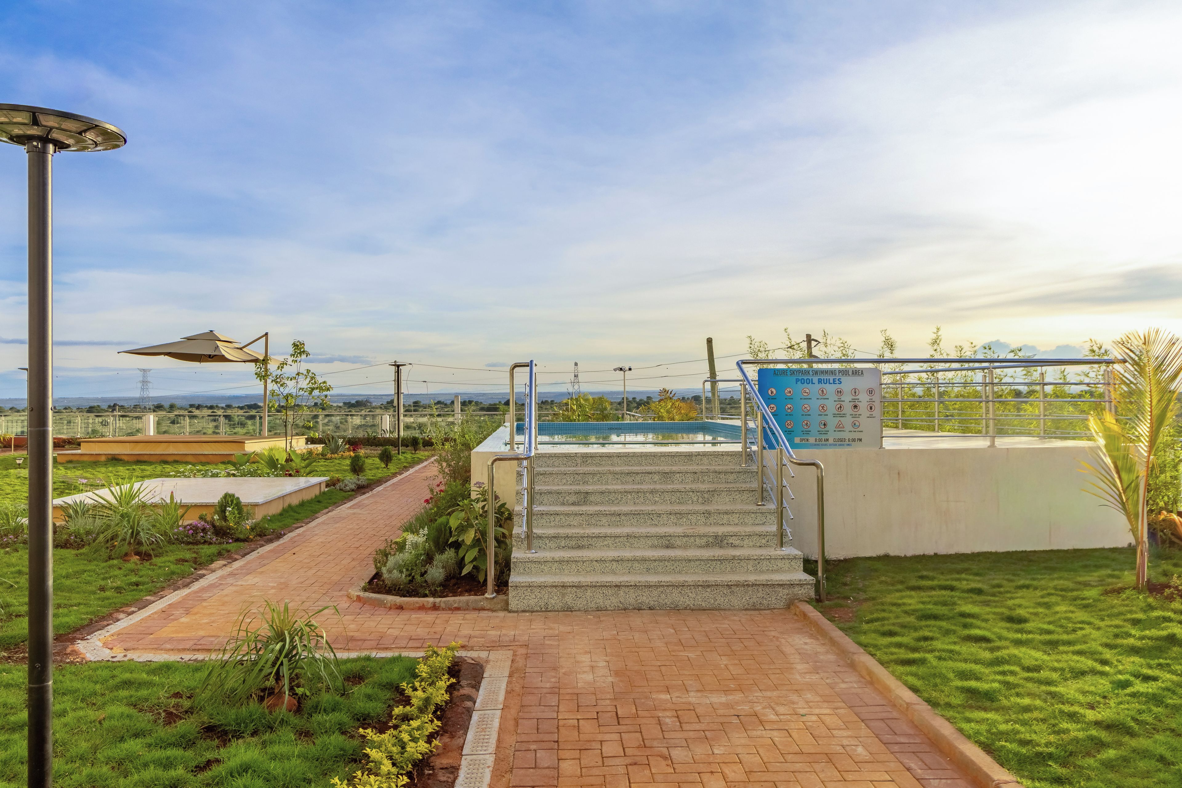 Área da piscina com uma placa detalhando as regras, uma escadaria de acesso e vista da paisagem ao redor.