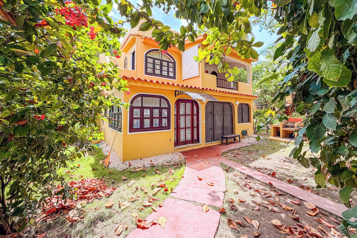 Uma casa de dois andares com porta vermelha, janelas grandes e uma varanda.
