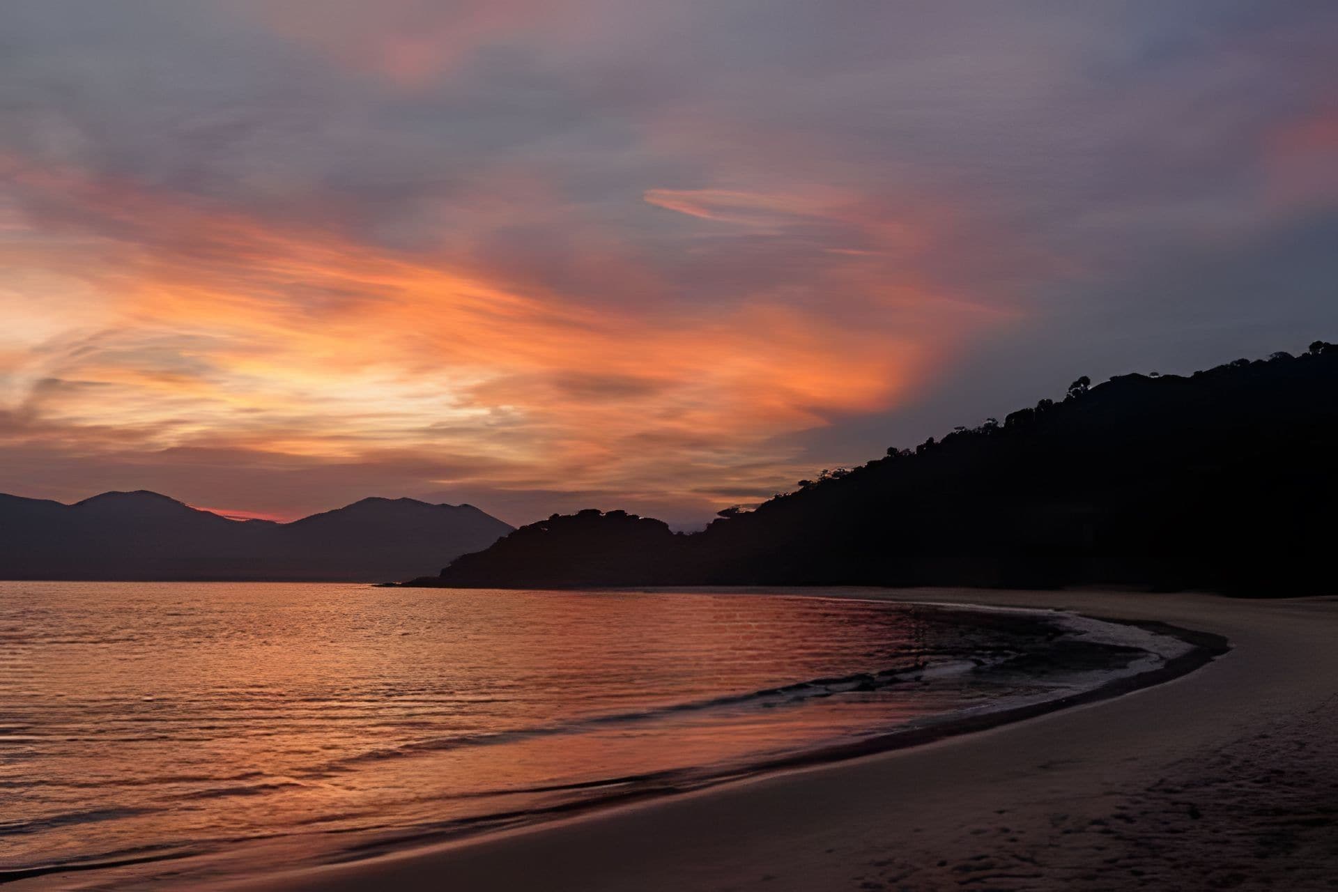 Uma praia com mar calmo e céu ao pôr do sol.