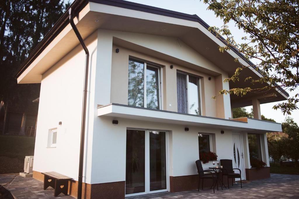 Uma casa moderna de dois andares com varanda, grandes janelas e área de pátio.