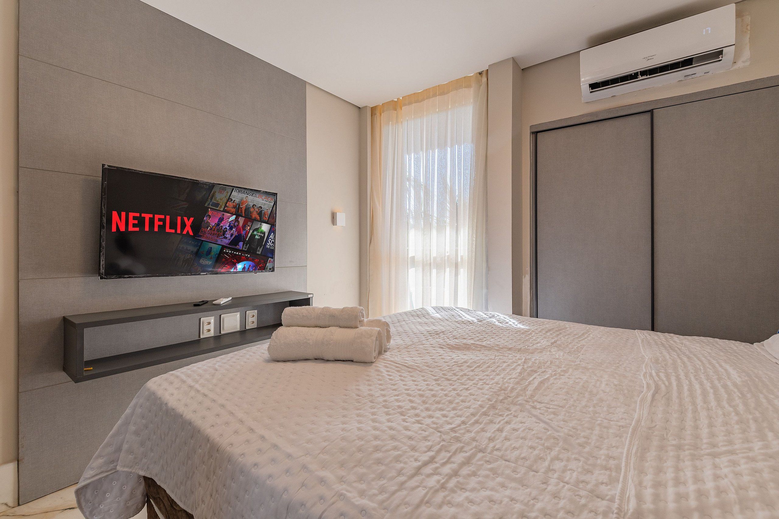 Quarto de hotel com cama, televisão na parede, guarda-roupa e ar condicionado.