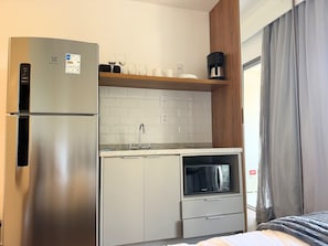 Uma cozinha compacta equipada com geladeira, micro-ondas e cafeteira.