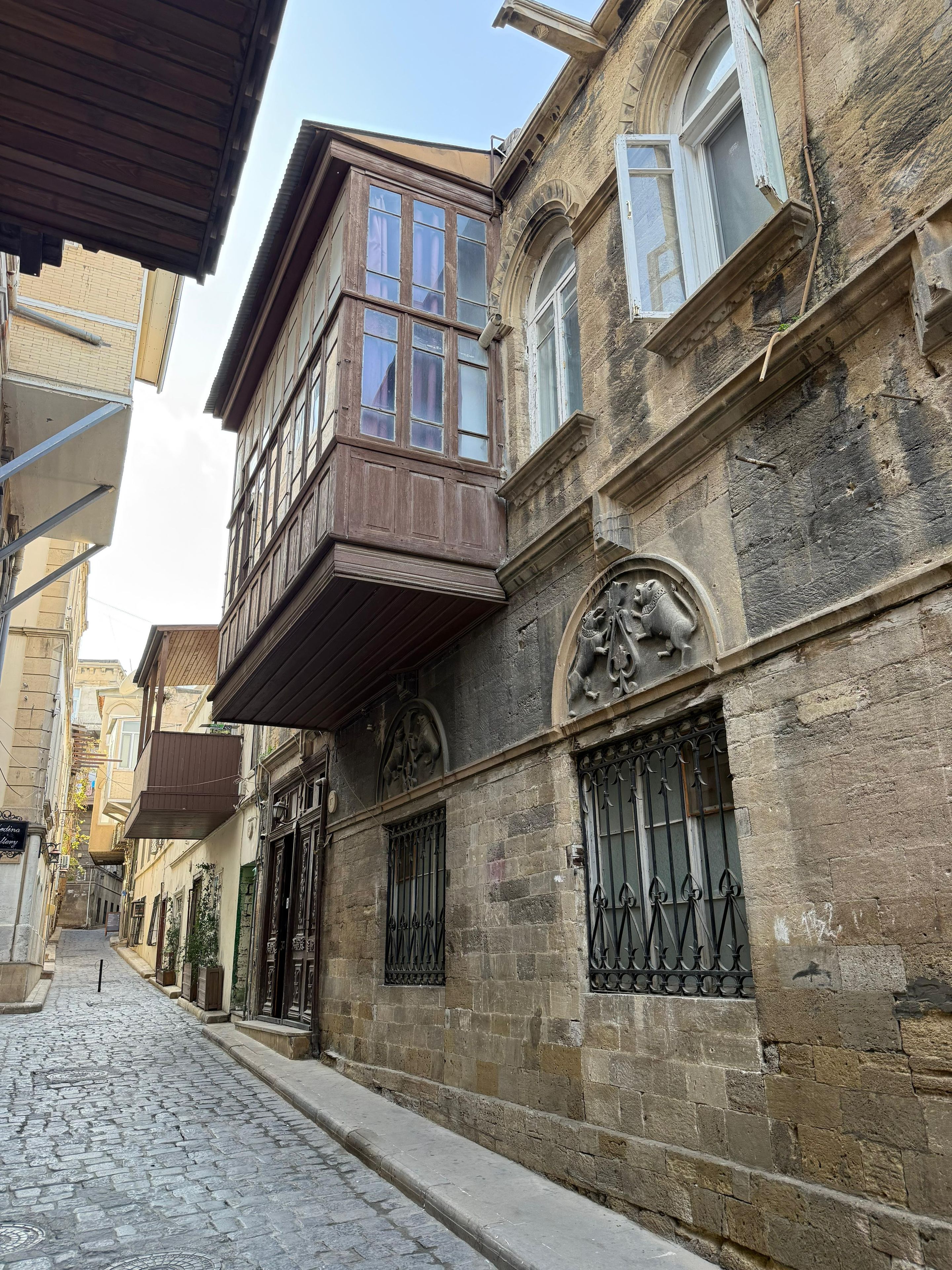 Uma rua estreita de paralelepípedos ladeada por edifícios históricos de pedra, com varandas e detalhes elaborados nas janelas.