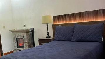 Quarto com uma cama grande, mesa de cabeceira, abajur e lareira.