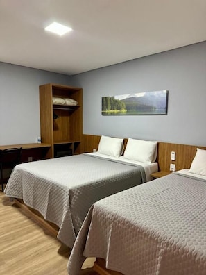 Quarto de hotel com duas camas, uma escrivaninha e um guarda-roupa.