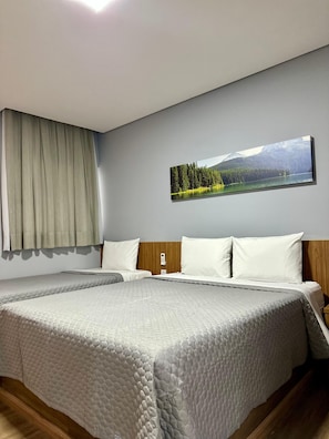 Quarto de hotel com duas camas, uma janela grande com cortinas, um quadro pendurado na parede e uma cabeceira de madeira.
