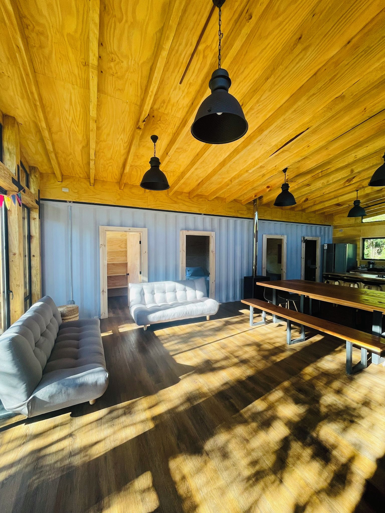 Um quarto amplo com teto de madeira, um sofá, uma mesa de jantar e uma área de cozinha.
