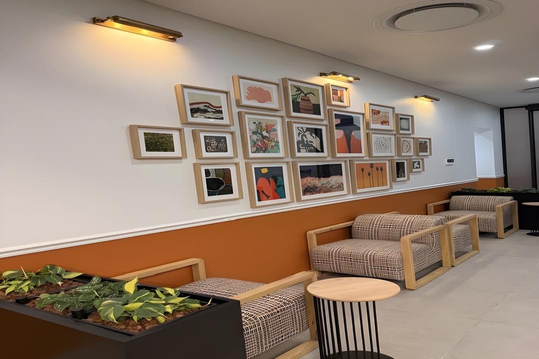 Uma área de espera com obras de arte emolduradas na parede, assentos acolchoados e um vaso de plantas.
