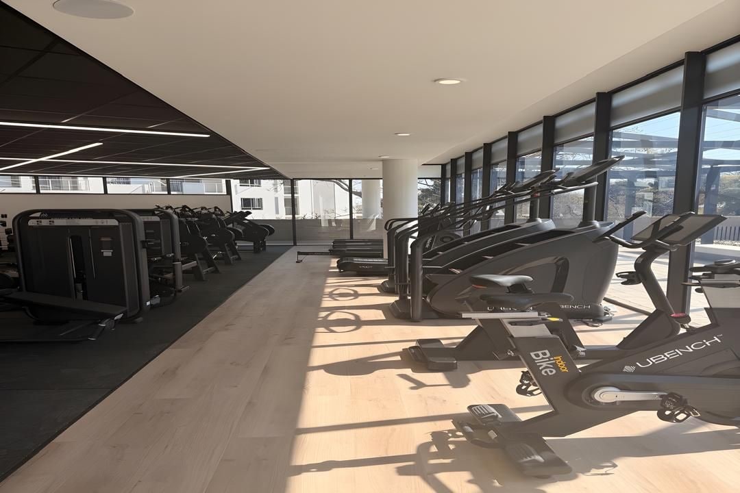 Uma academia com equipamentos de ginástica, amplas janelas e piso de madeira.