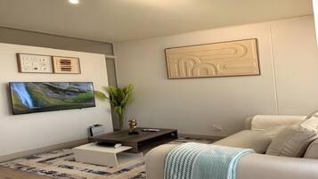 Uma sala de estar moderna com televisão de tela plana, mesinha de centro, sofá e planta decorativa.