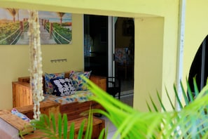 Um banco de madeira com almofada floral, um gancho preso à parede e uma porta que dá para um quarto com um laptop sobre uma mesa.