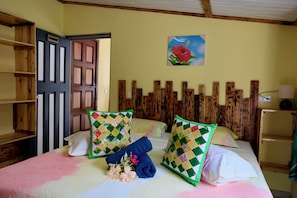 Quarto com cama, cabeceira de madeira, pintura de uma flor e prateleira com abajur.