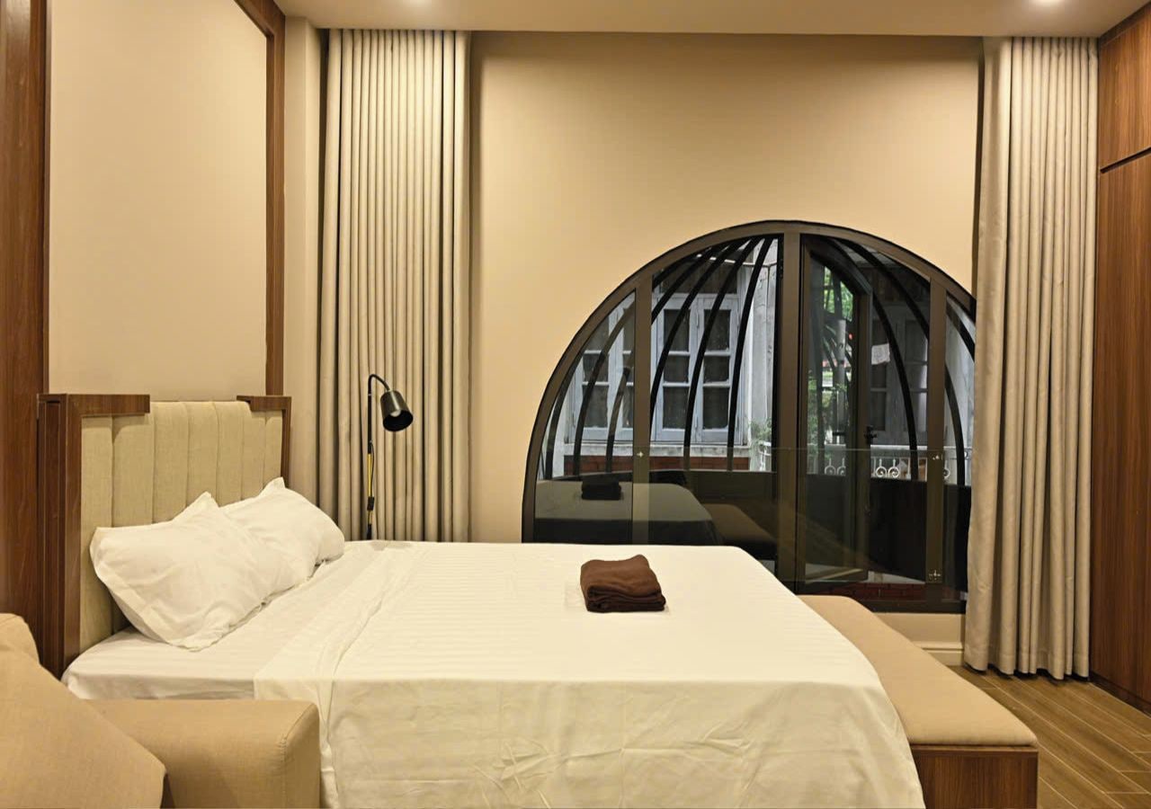 Quarto de hotel com cama, mesa de cabeceira, luminária e janela com vista para o exterior.
