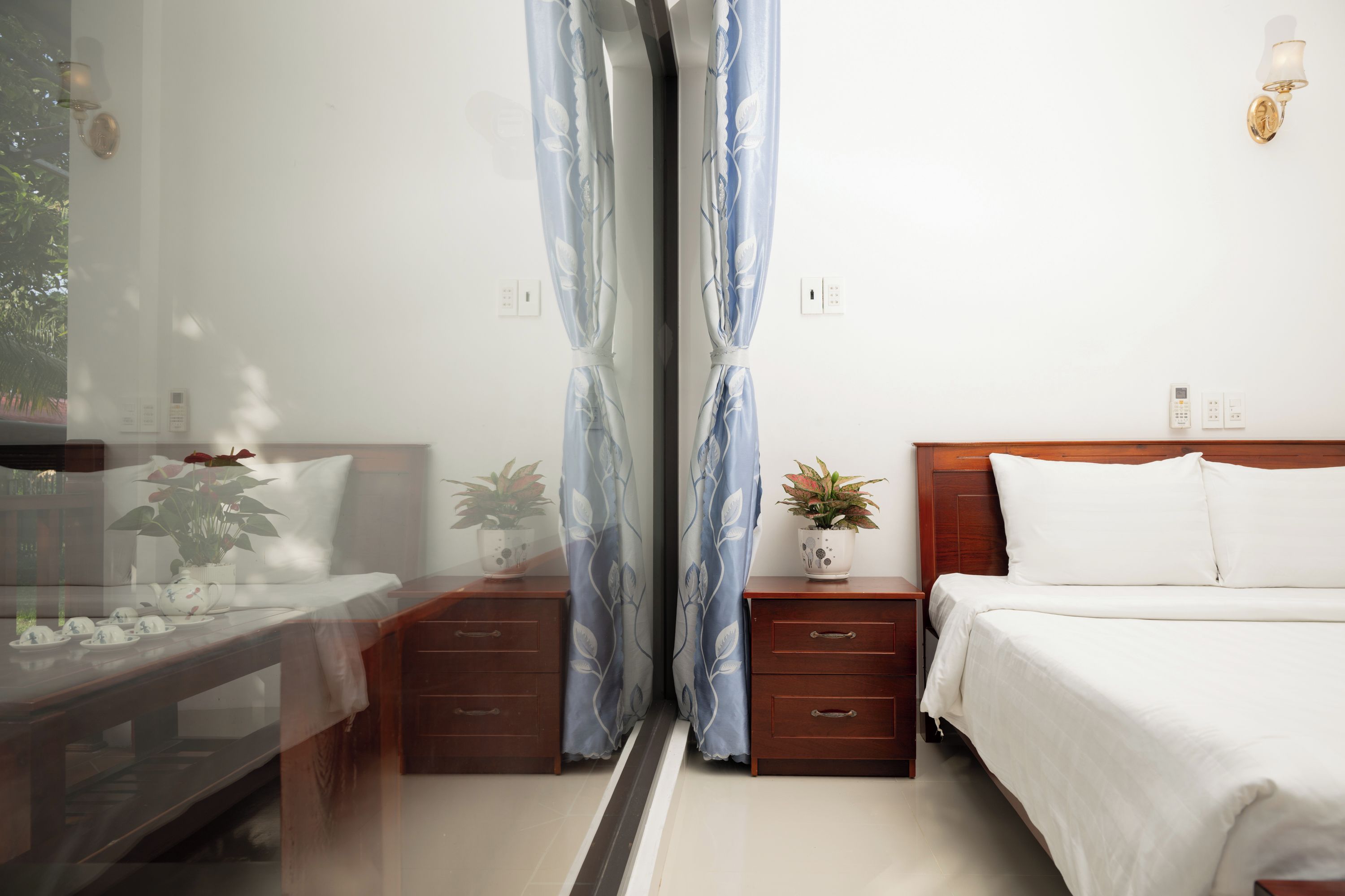 Quarto de hotel com cama, duas mesas de cabeceira, um criado-mudo, um espelho e janela com cortinas.
