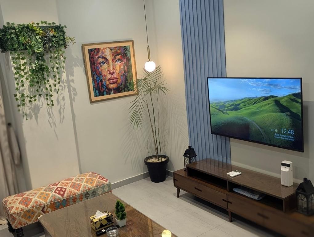 Uma sala de estar moderna com televisão de tela plana, sofá, mesa de centro, planta em vaso e prateleira fixada na parede.