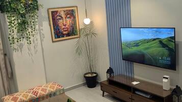 Uma sala de estar moderna com televisão de tela plana, sofá, mesa de centro, planta em vaso e prateleira fixada na parede.