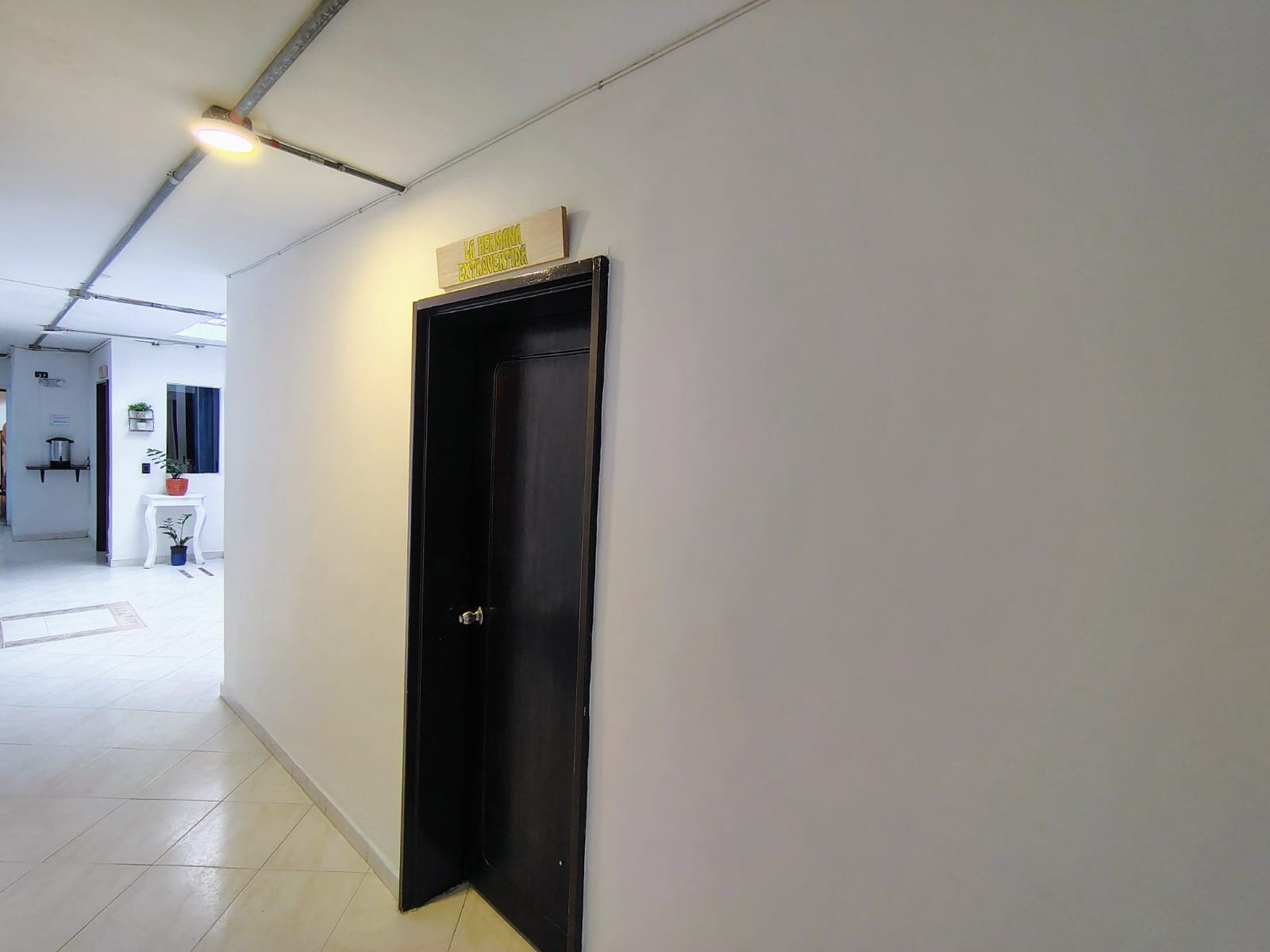 Um corredor com uma porta preta, uma placa acima e uma planta em vaso sobre uma mesa console branca.