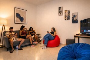Uma sala de estar moderna com um sofá, um puff vermelho, uma televisão e arte abstrata nas paredes.