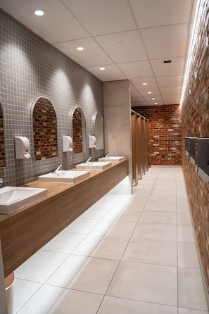 Casa de banho moderna com várias pias, secadores de mãos e design de parede de tijolo.