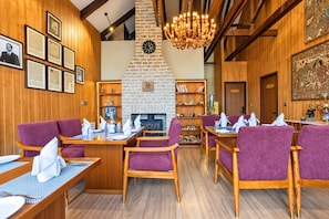 Um restaurante com paredes de madeira, lareira de tijolos e cadeiras estofadas em roxo.