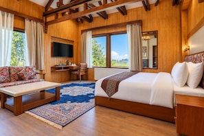 Quarto com cama, sofá, escrivaninha e televisão.