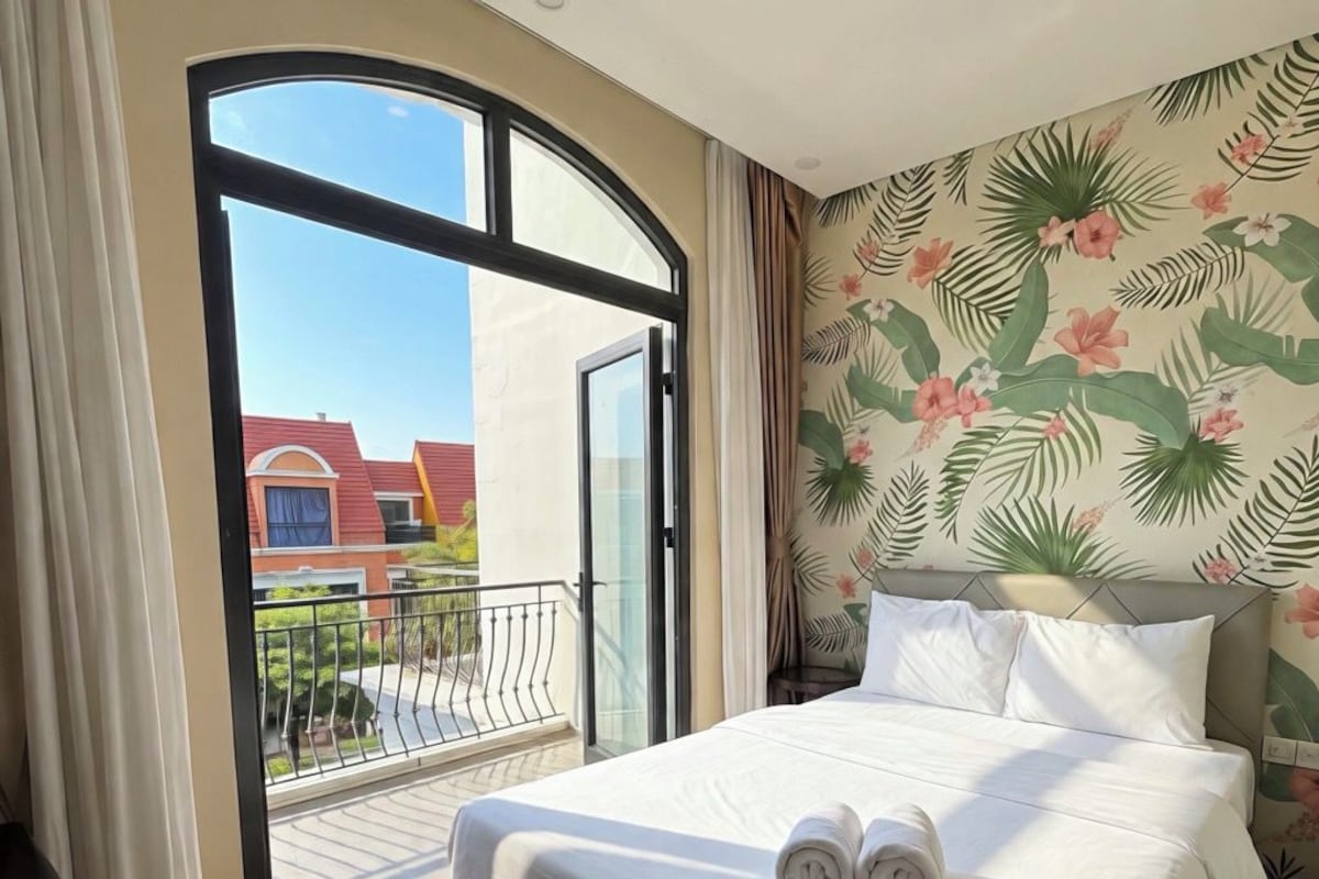 Quarto de hotel com cama, varanda e papel de parede tropical.