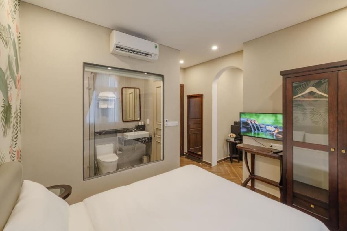 Quarto de hotel com cama, televisão, banheiro com espelho e ar condicionado.
