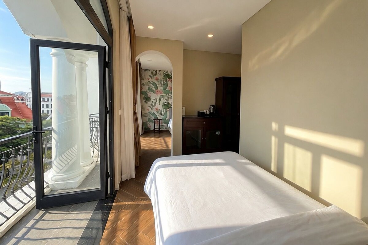 Quarto de hotel com varanda, cama, escrivaninha e vista para a paisagem urbana.