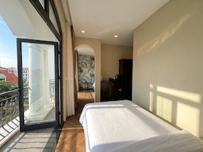 Quarto de hotel com varanda, cama, escrivaninha e vista para a paisagem urbana.