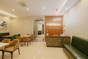 Interior de restaurante com balcão de recepção, área de estar e sofá verde.