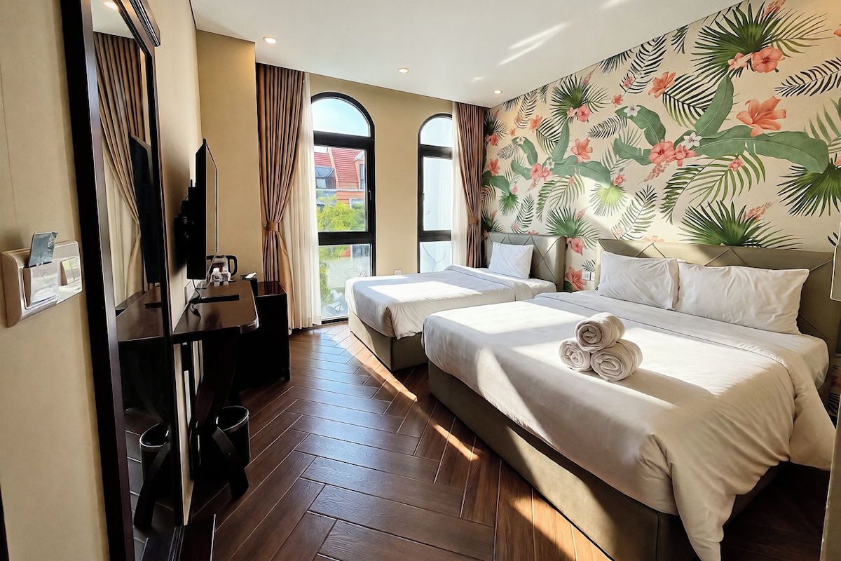 Quarto de hotel com duas camas, televisão, escrivaninha e janela com cortinas.