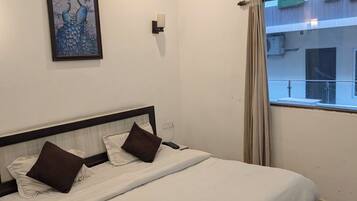 Quarto de hotel com cama, ar-condicionado fixado na parede, janela com cortinas e uma obra de arte emoldurada na parede.