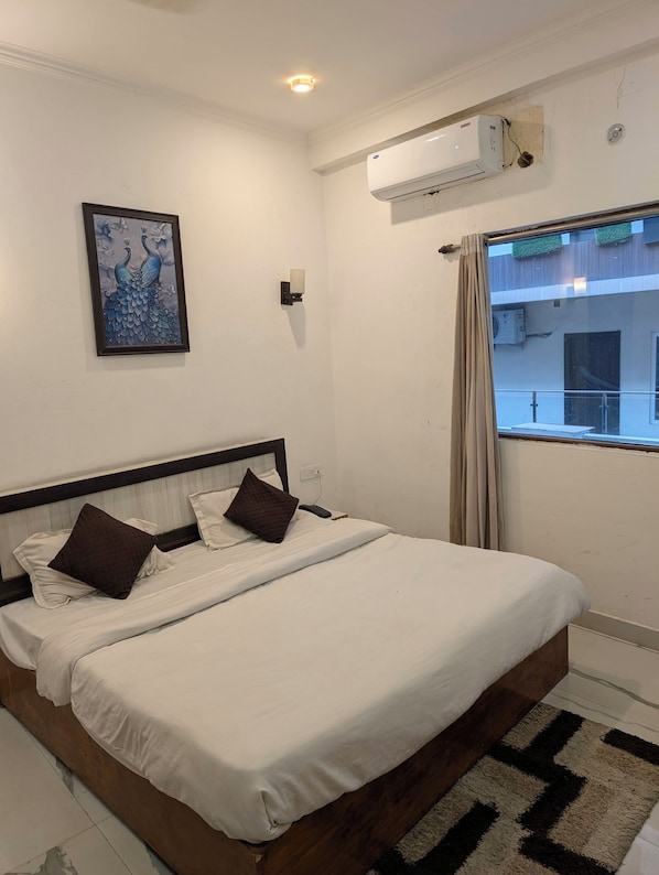 Quarto de hotel com cama, ar-condicionado fixado na parede, janela com cortinas e uma obra de arte emoldurada na parede.