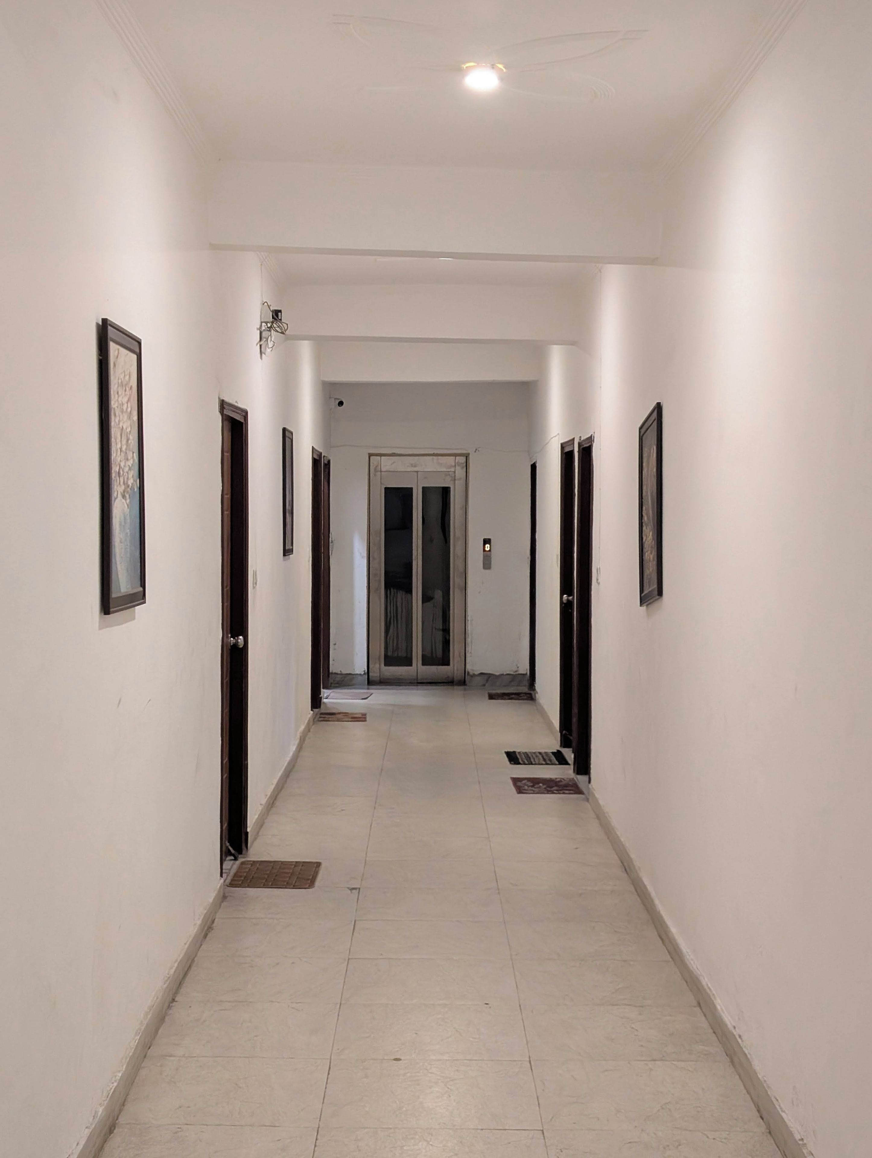 Corredor com portas em ambos os lados, piso ladrilhado e iluminação no teto.