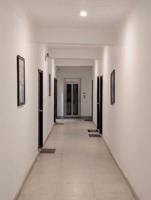Corredor com portas em ambos os lados, piso ladrilhado e iluminação no teto.