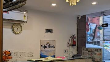 Balcão de recepção de hotel com um candelabro, um relógio e uma placa para Vajra Hotels.