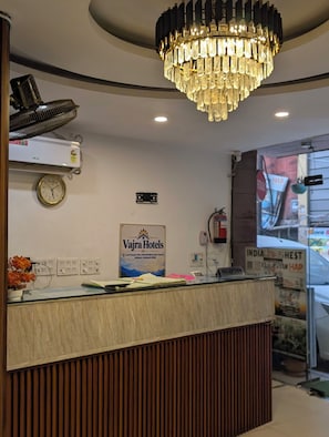 Balcão de recepção de hotel com um candelabro, um relógio e uma placa para Vajra Hotels.