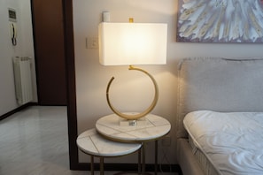Quarto de hotel com uma cama, uma mesa de cabeceira com luminária e um quadro na parede.