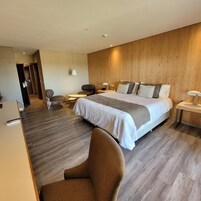 Quarto de hotel com uma cama grande, escrivaninha, cadeira e painel de parede em madeira.
