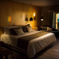 Quarto de hotel com uma cama grande, mesa de cabeceira, luminária e vista para o exterior.