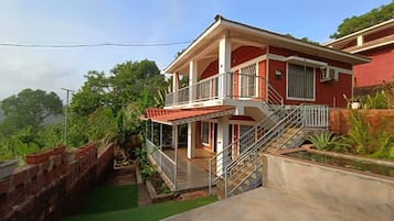 Uma casa de dois andares com varanda, escada e um pequeno jardim.