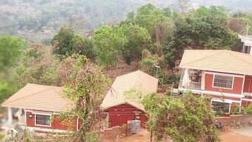 Área residencial com casas de paredes vermelhas e telhados em cerâmica, rodeada por vegetação e relevo montanhoso.