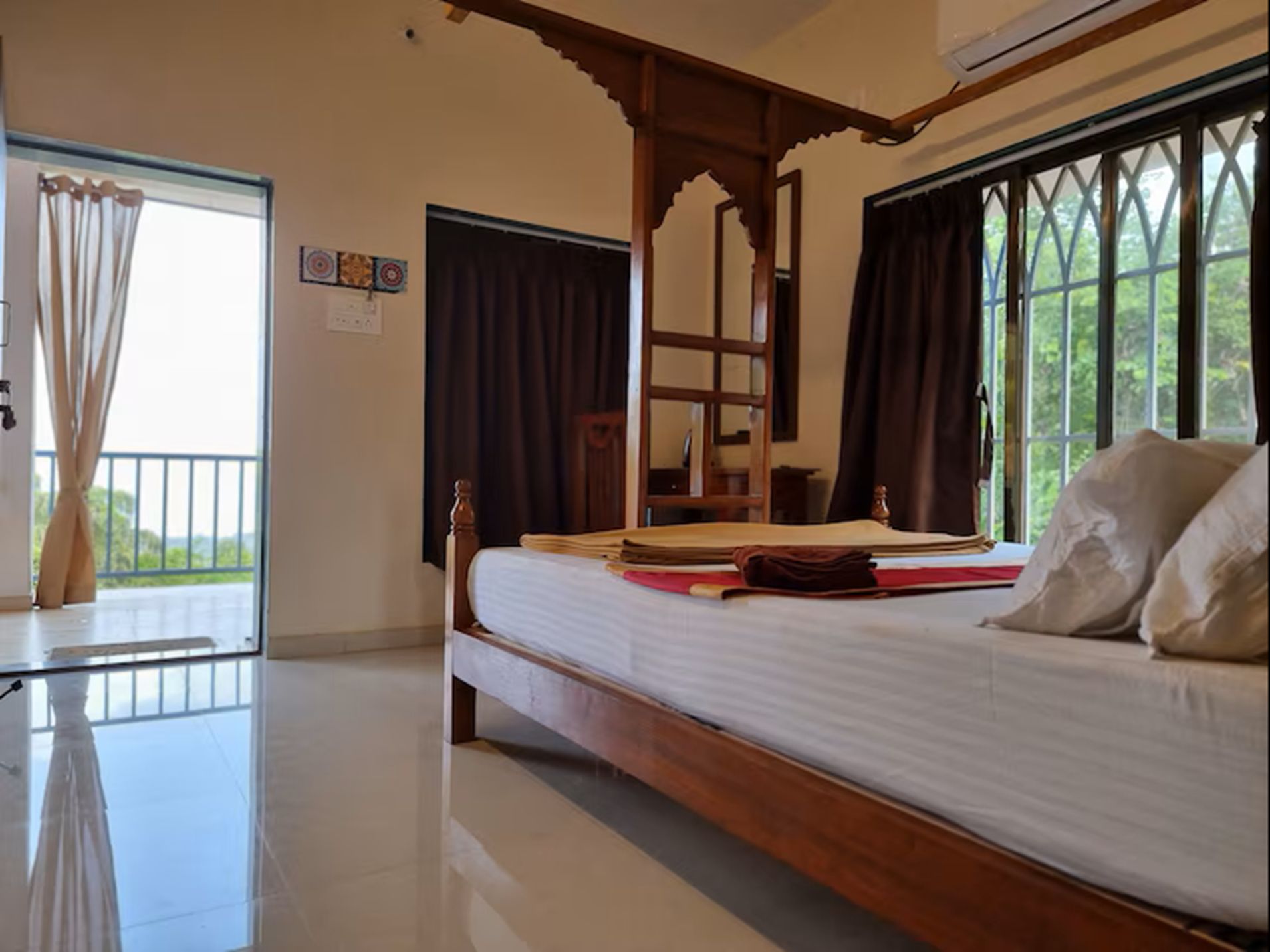 Quarto com cama de madeira, porta para varanda e vista para o verde lá fora.