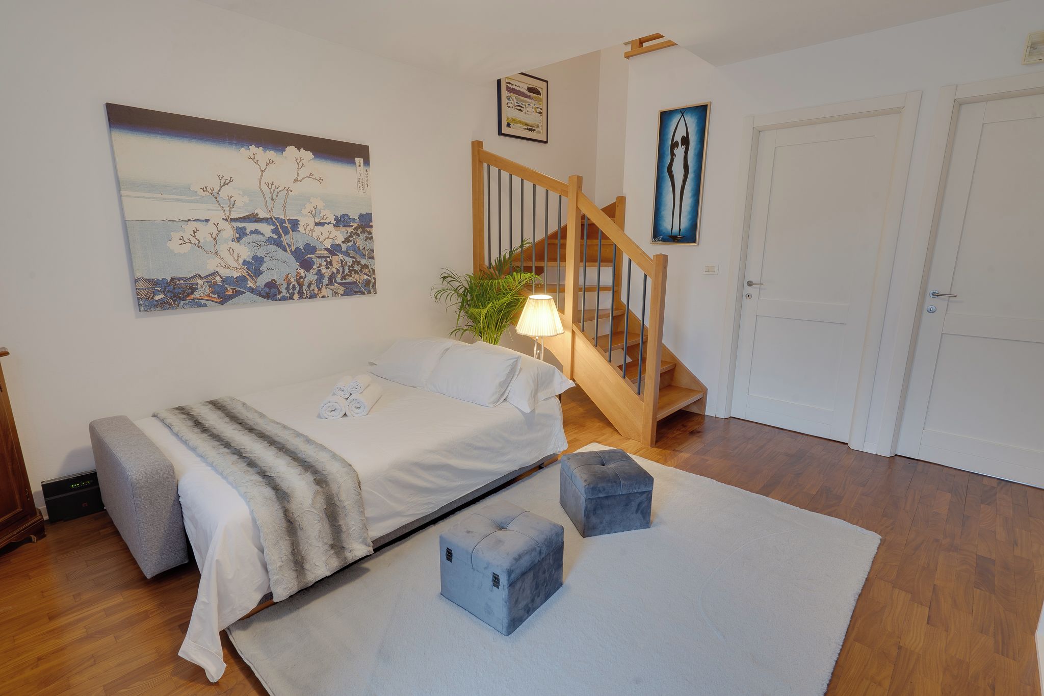 Quarto com cama, mesa de cabeceira, abajur, escada e porta.