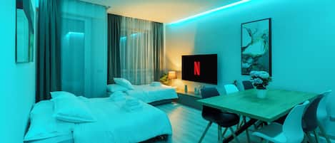 Quarto de hotel moderno com duas camas, uma TV, uma mesa de jantar e uma planta.