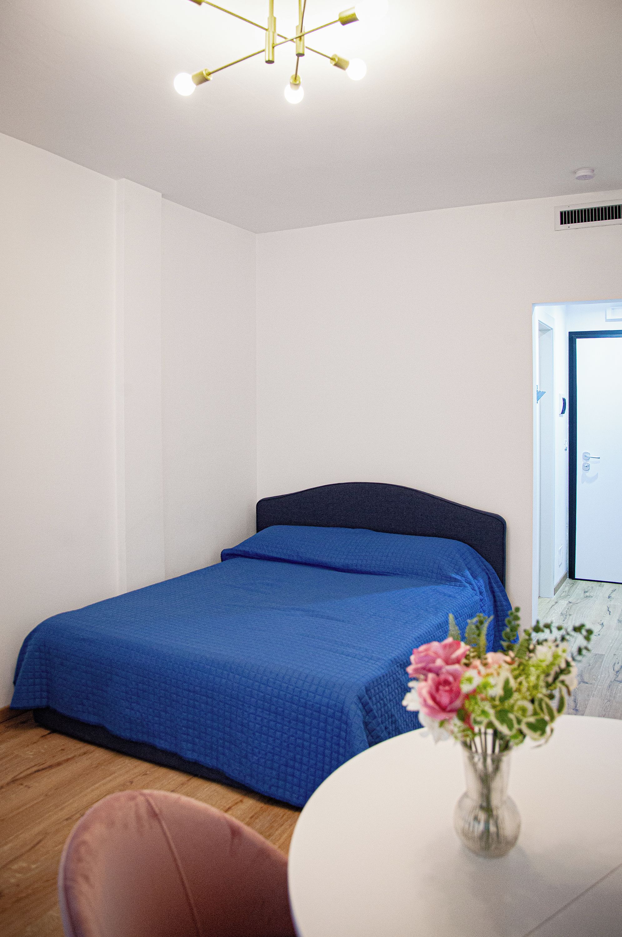 Quarto com cama, mesa de cabeceira com um vaso de flores e luminária no teto.