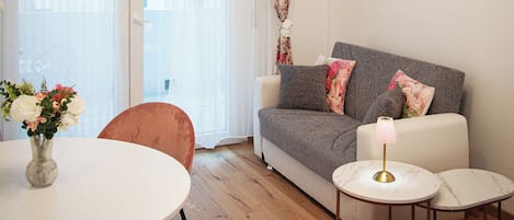 Sala de estar com sofá, duas mesas laterais, uma mesinha redonda e um vaso com flores.