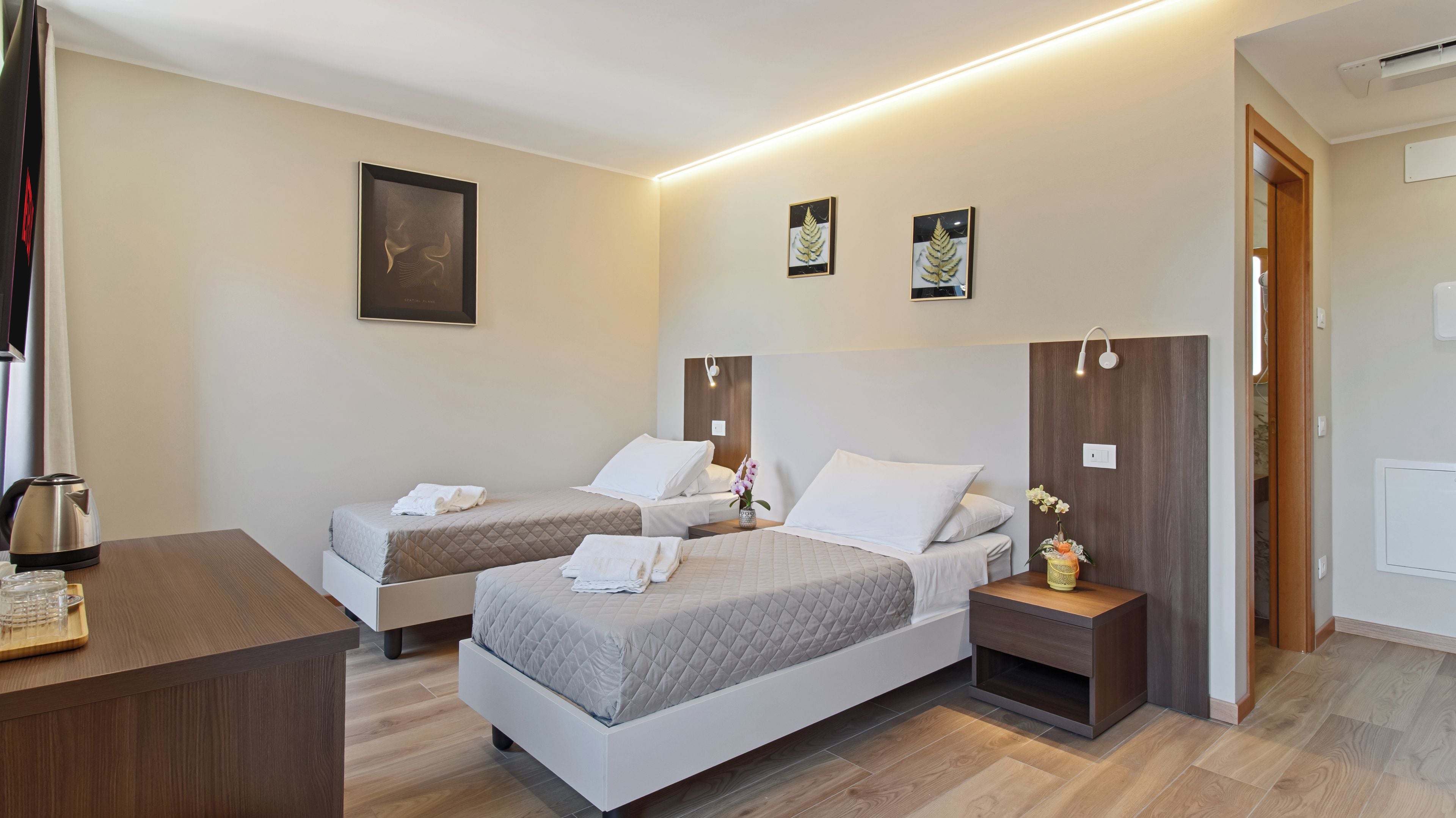 Quarto de hotel com duas camas, uma escrivaninha e uma mesinha de cabeceira.