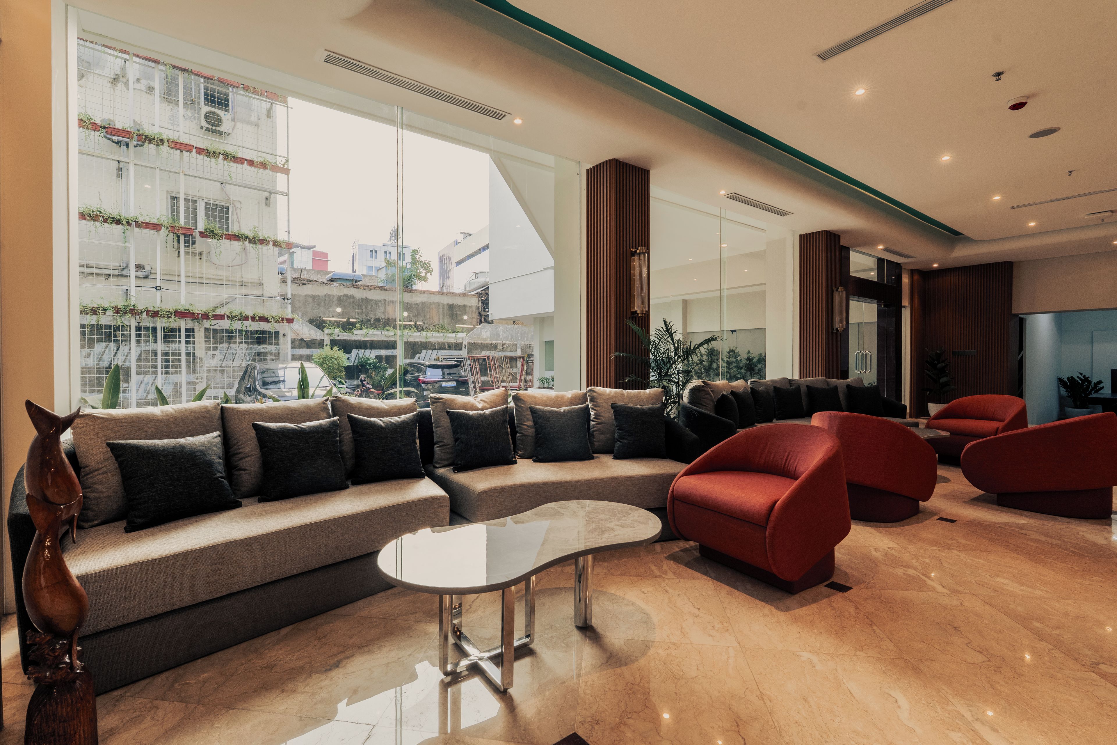 Um lobby moderno com sofá modular, poltronas vermelhas, mesa de centro de vidro e grandes janelas com vista para a cidade.